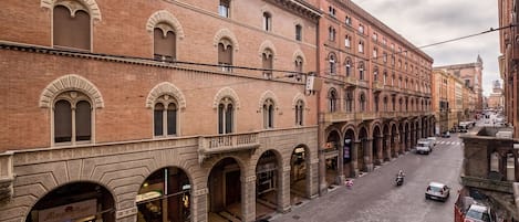 Vista da rua de um edifício histórico com janelas em arco e uma fileira de lojas no andar térreo.