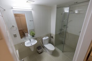 Casa de banho moderna com chuveiro em cabine de vidro, sanita, lavatório e espelho.