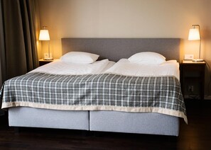 Uma cama de casal com cabeceira cinza, duas luminárias de cabeceira e um edredom xadrez.