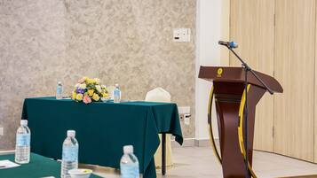 Sala de conferência com uma mesa coberta por uma toalha azul-turquesa, um pódio e garrafas de água.