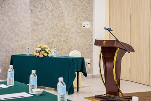 Sala de conferência com uma mesa coberta por uma toalha azul-turquesa, um pódio e garrafas de água.