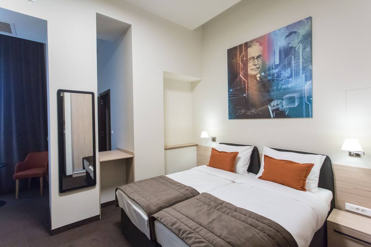 Quarto de hotel com uma cama grande, duas mesas de cabeceira, uma escrivaninha, uma cadeira e um quadro grande na parede.