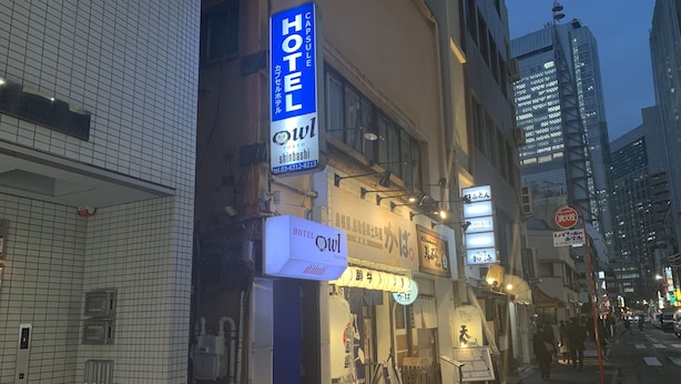 Um hotel com uma placa azul, uma placa com caracteres japoneses e uma fachada com cerca de madeira.