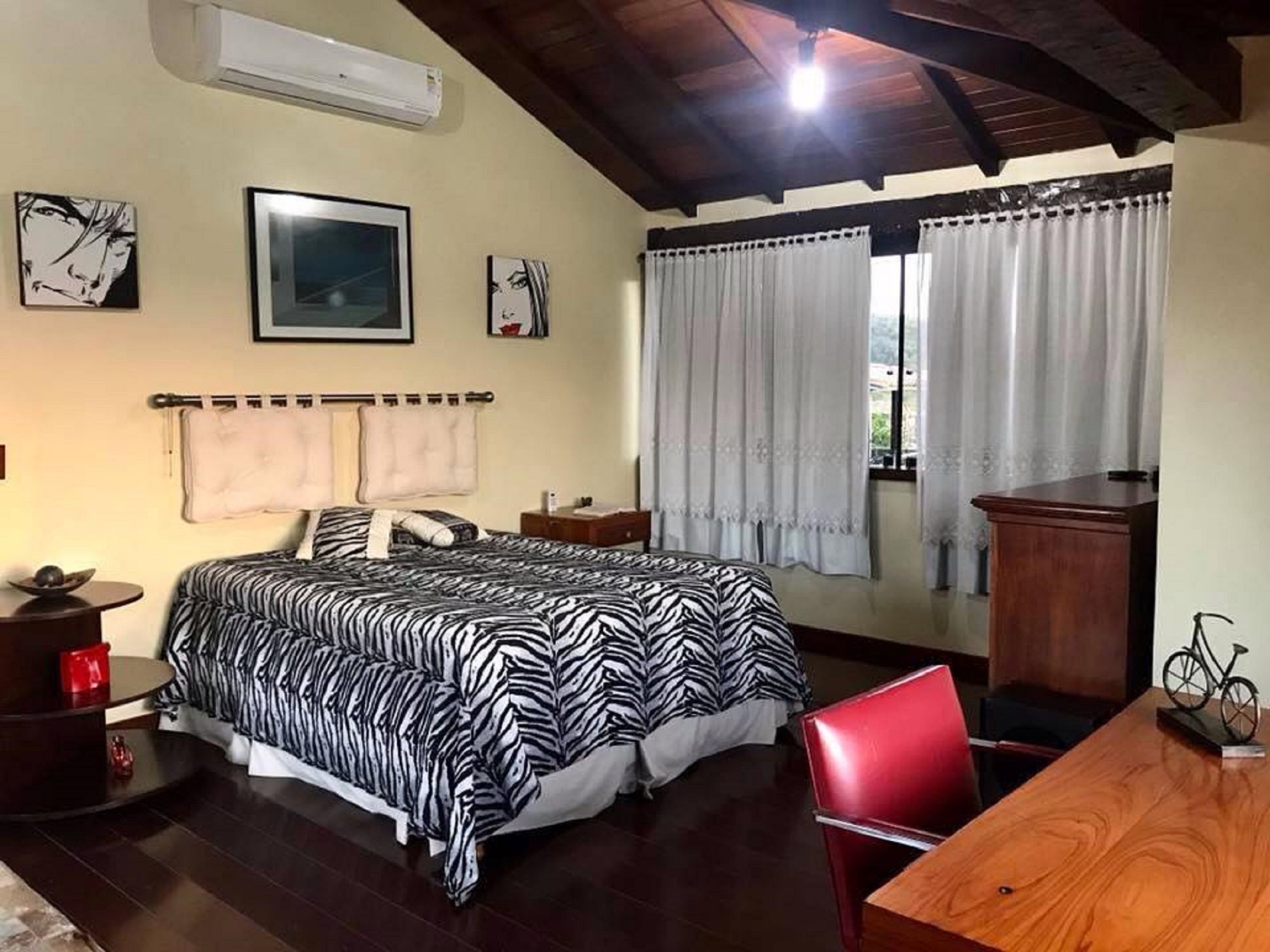 Quarto com cama, escrivaninha, cadeira, radiador e janela com cortinas.