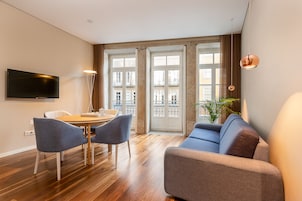 Uma sala de estar moderna com piso de madeira, um sofá, uma mesa de jantar com cadeiras e uma TV fixada na parede.
