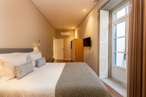 Quarto de hotel com uma cama grande, televisão de tela plana na parede e janela com cortinas.
