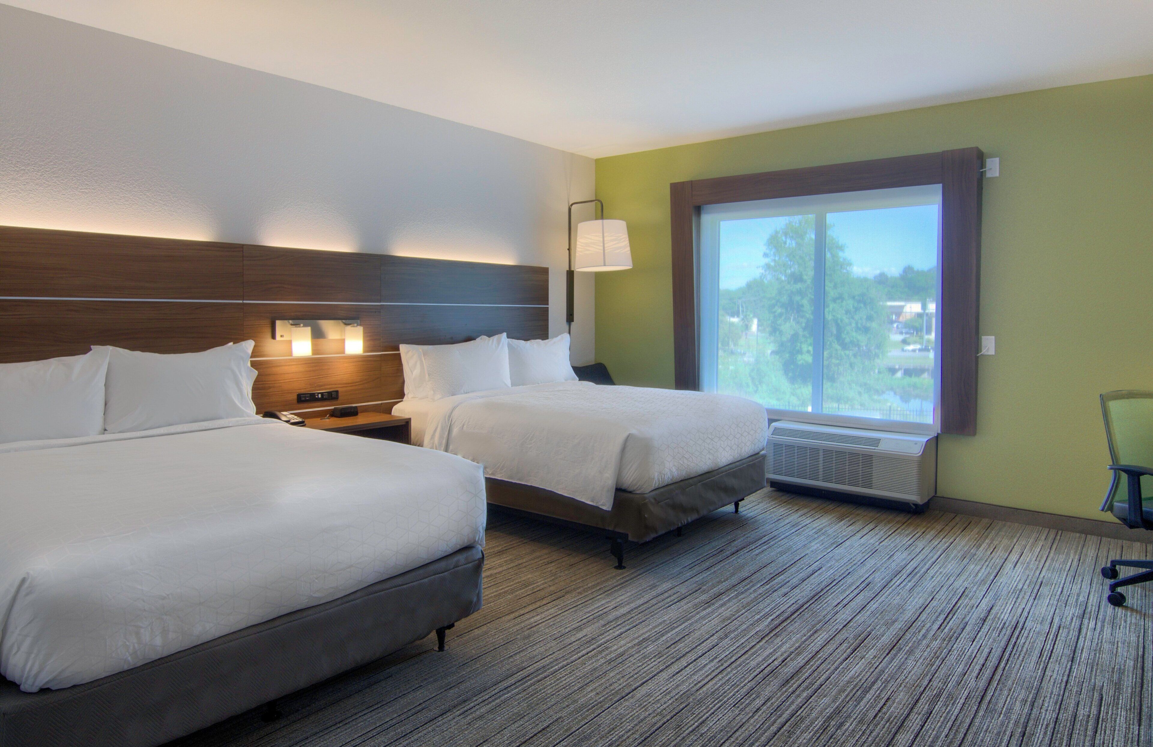 Quarto de hotel com duas camas, uma mesa de cabeceira, um abajur, uma janela e um radiador.