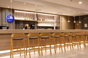 Uma área de bar moderna com um balcão comprido, vários banquetas e uma variedade de garrafas na prateleira.