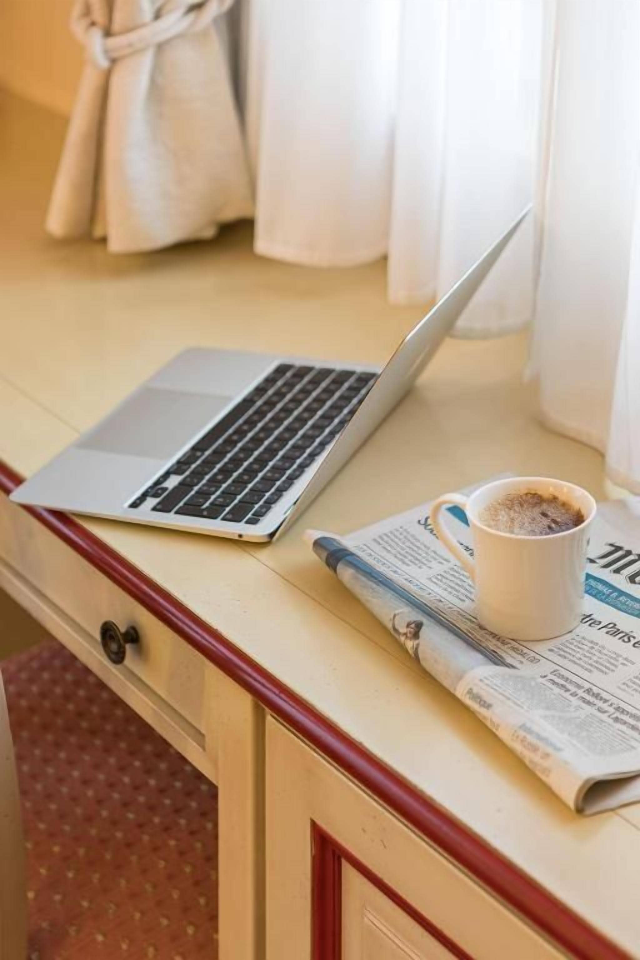 Um laptop sobre uma mesa, com uma xícara de café e um jornal.