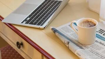 Um laptop sobre uma mesa, com uma xícara de café e um jornal.