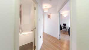 Um corredor com piso de madeira, uma porta branca que dá para um banheiro e uma área de jantar com cadeiras e uma mesa.