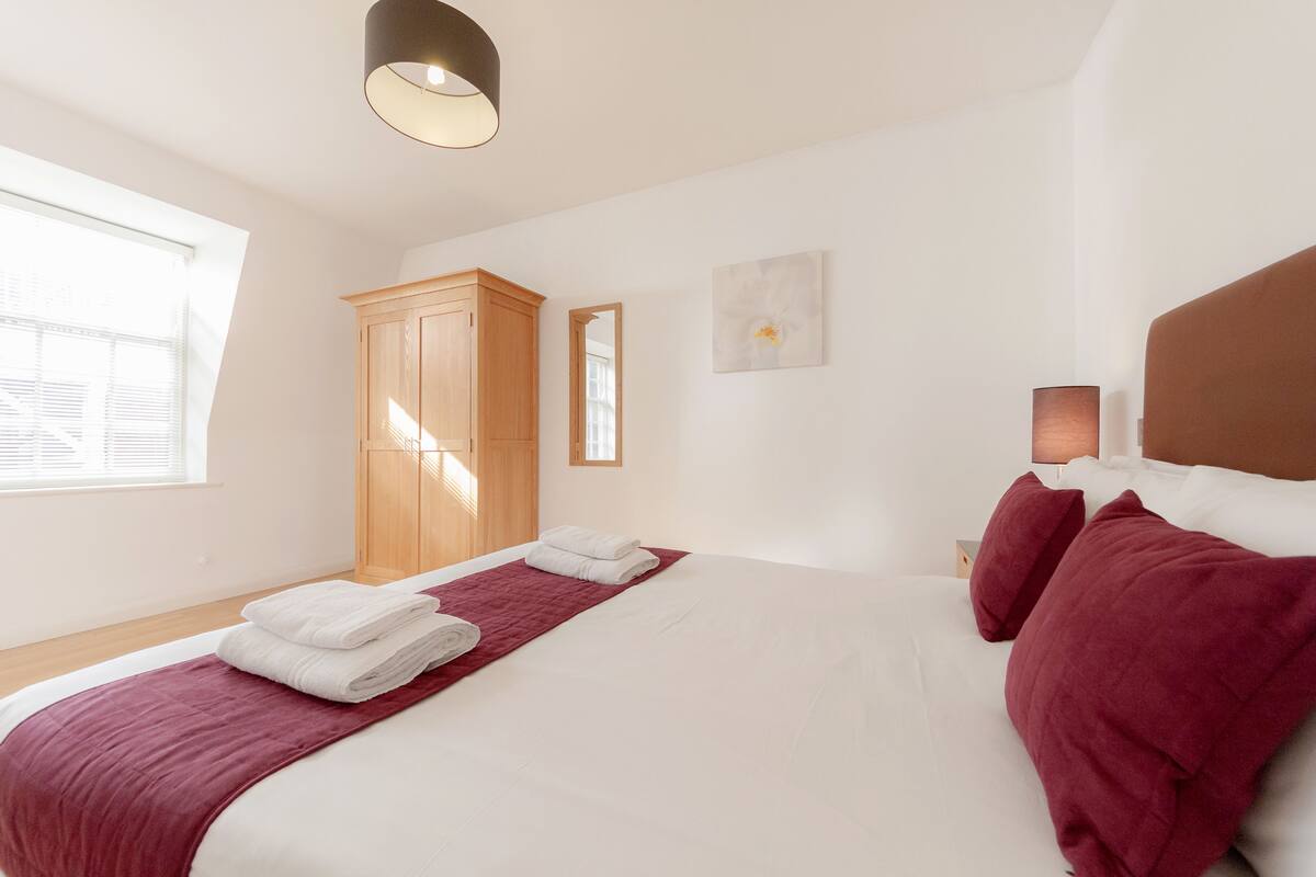 Quarto de hotel com uma cama grande, um guarda-roupa de madeira, um espelho e uma janela com persianas.