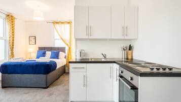 Quarto de hotel moderno com cama, pequeno espaço de cozinha e banheiro.