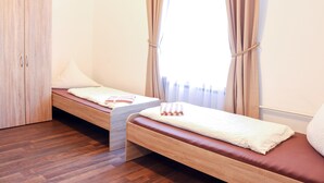 Quarto com duas camas de solteiro, guarda-roupa de madeira e janela com cortinas.