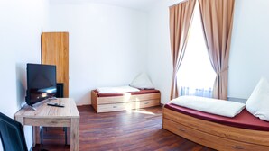 Quarto moderno com escrivaninha de madeira, cama com colchão vermelho, televisão e janela com cortinas.
