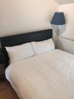 Cama bem arrumada com lençóis brancos num quarto com cabeceira preta e radiador branco.