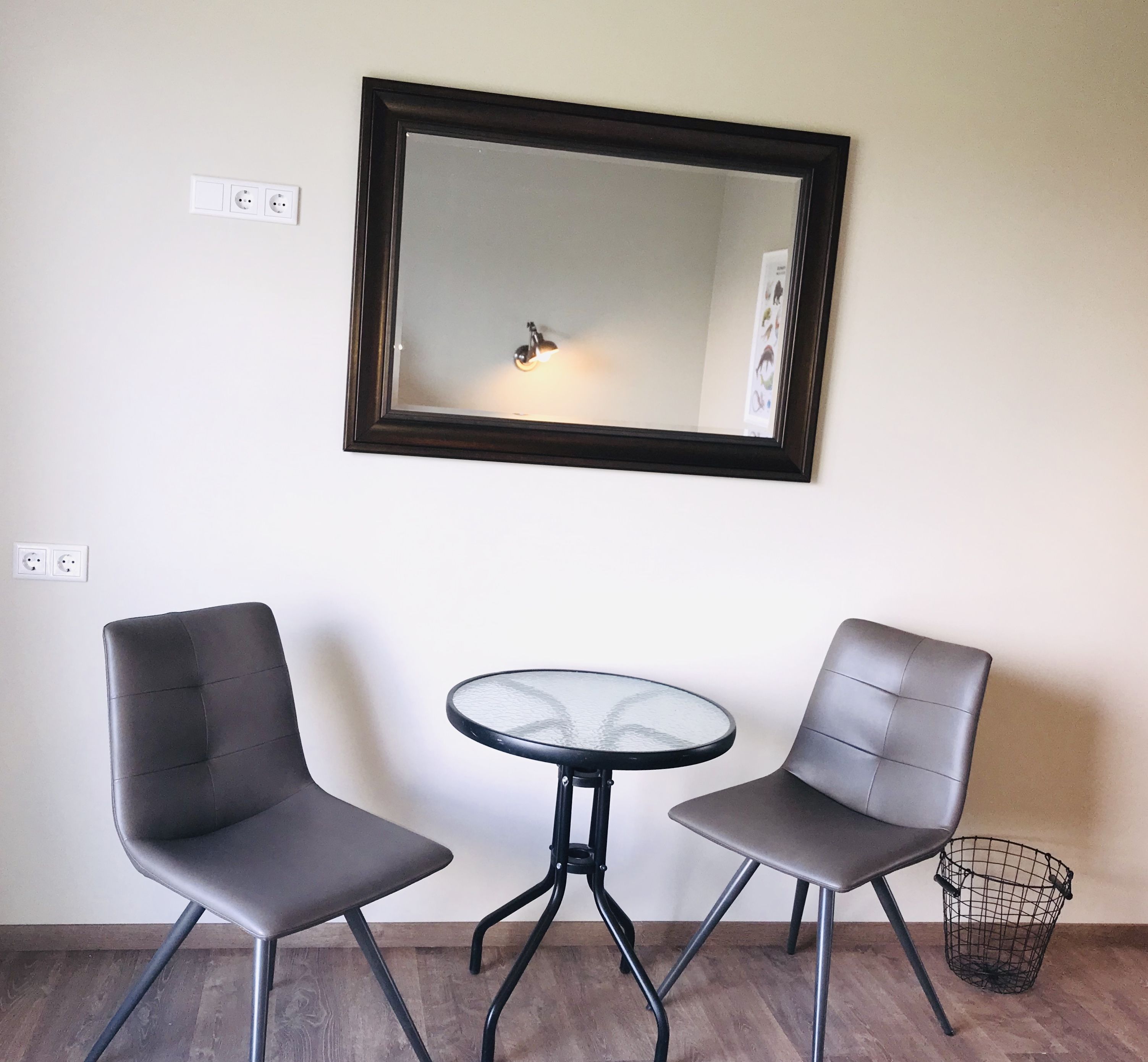 Quarto com duas cadeiras, uma mesa redonda pequena, um espelho na parede e uma tomada.
