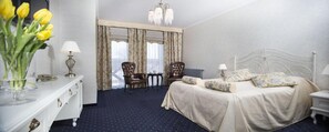 Quarto de hotel com cama, duas cadeiras, mesa pequena, cômoda e um vaso de flores.