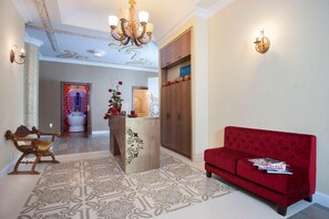 Um hall de hotel com um sofá vermelho, um balcão de recepção de madeira, um candelabro e um piso com padrão.