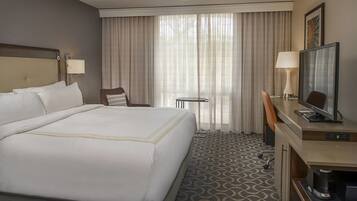 Quarto de hotel com uma cama grande, uma mesa com televisão, uma cadeira, uma mesinha e um abajur.