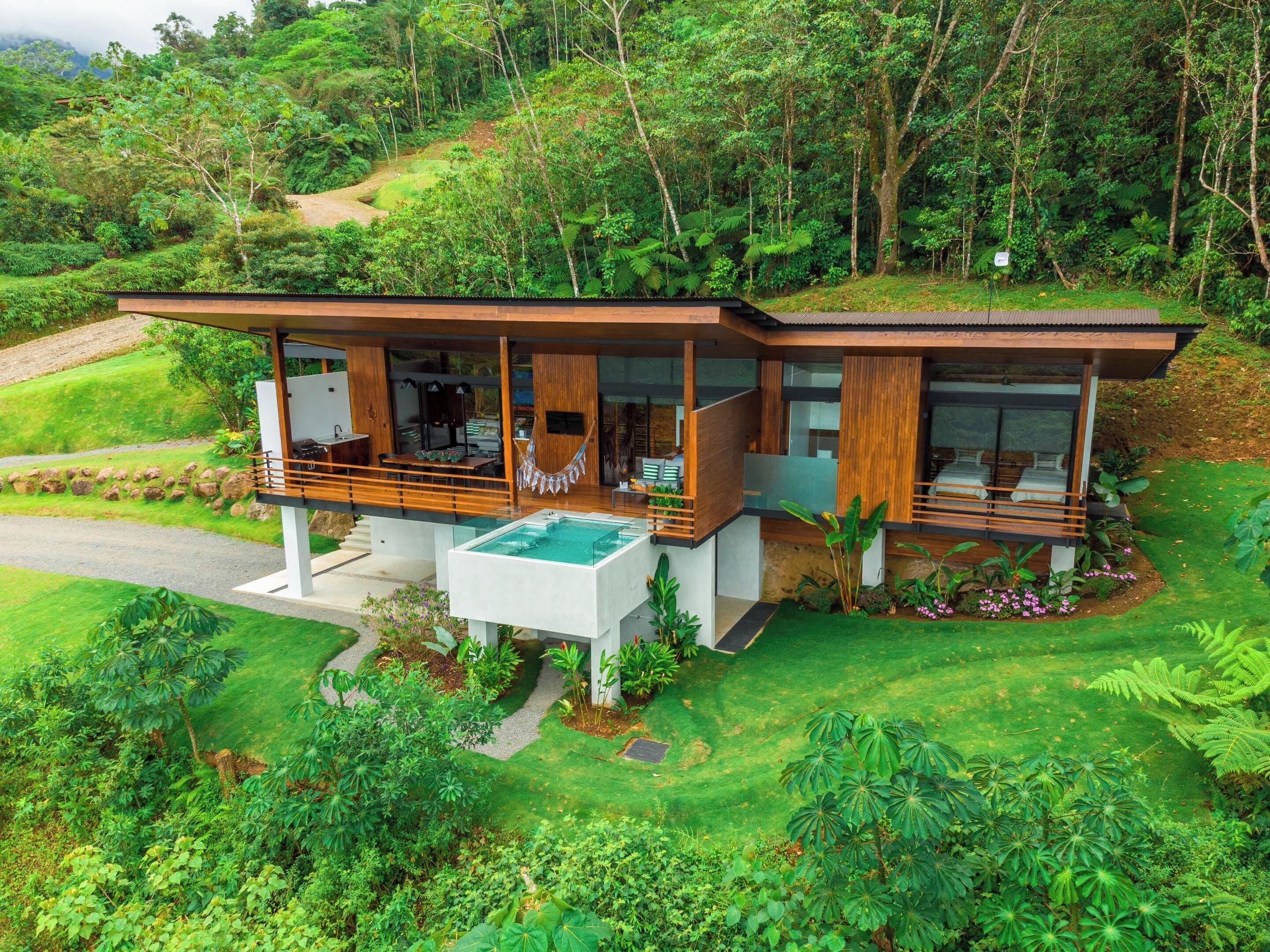 Uma casa moderna com piscina envidraçada, cercada por vegetação exuberante e paisagem montanhosa.