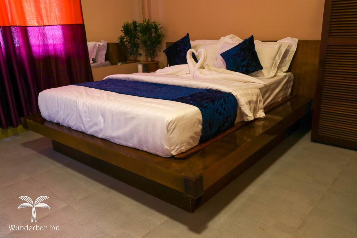 Quarto de hotel moderno com estrutura de cama de madeira, colcha azul e branca e travesseiro decorativo em formato de cisne.