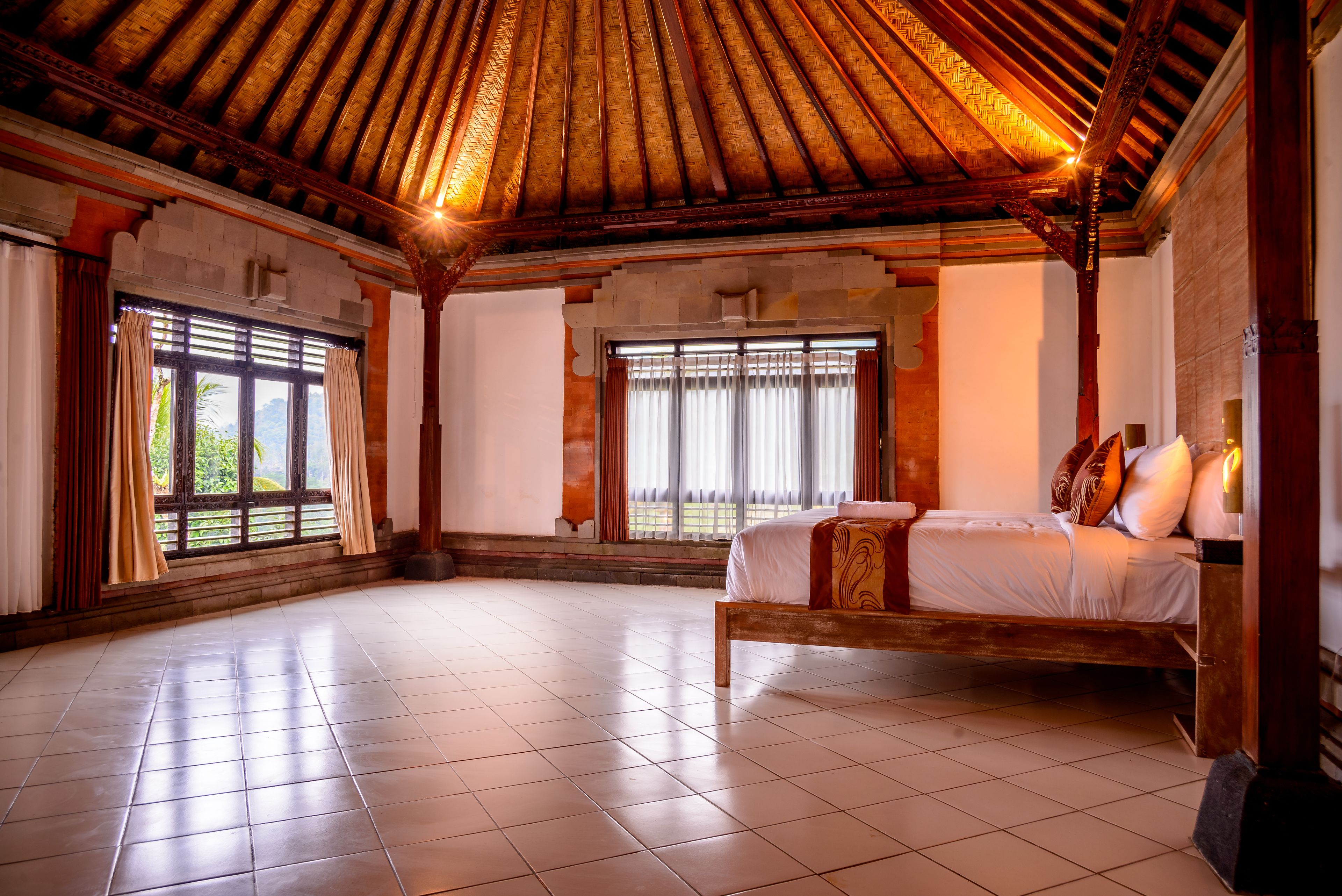 Um quarto espaçoso com uma cama grande, vigas de madeira no teto e amplas janelas com cortinas.