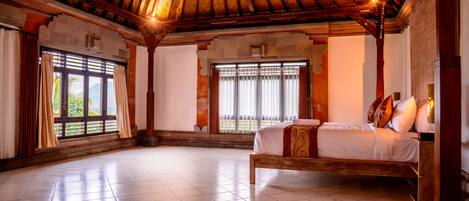 Um quarto espaçoso com uma cama grande, vigas de madeira no teto e amplas janelas com cortinas.