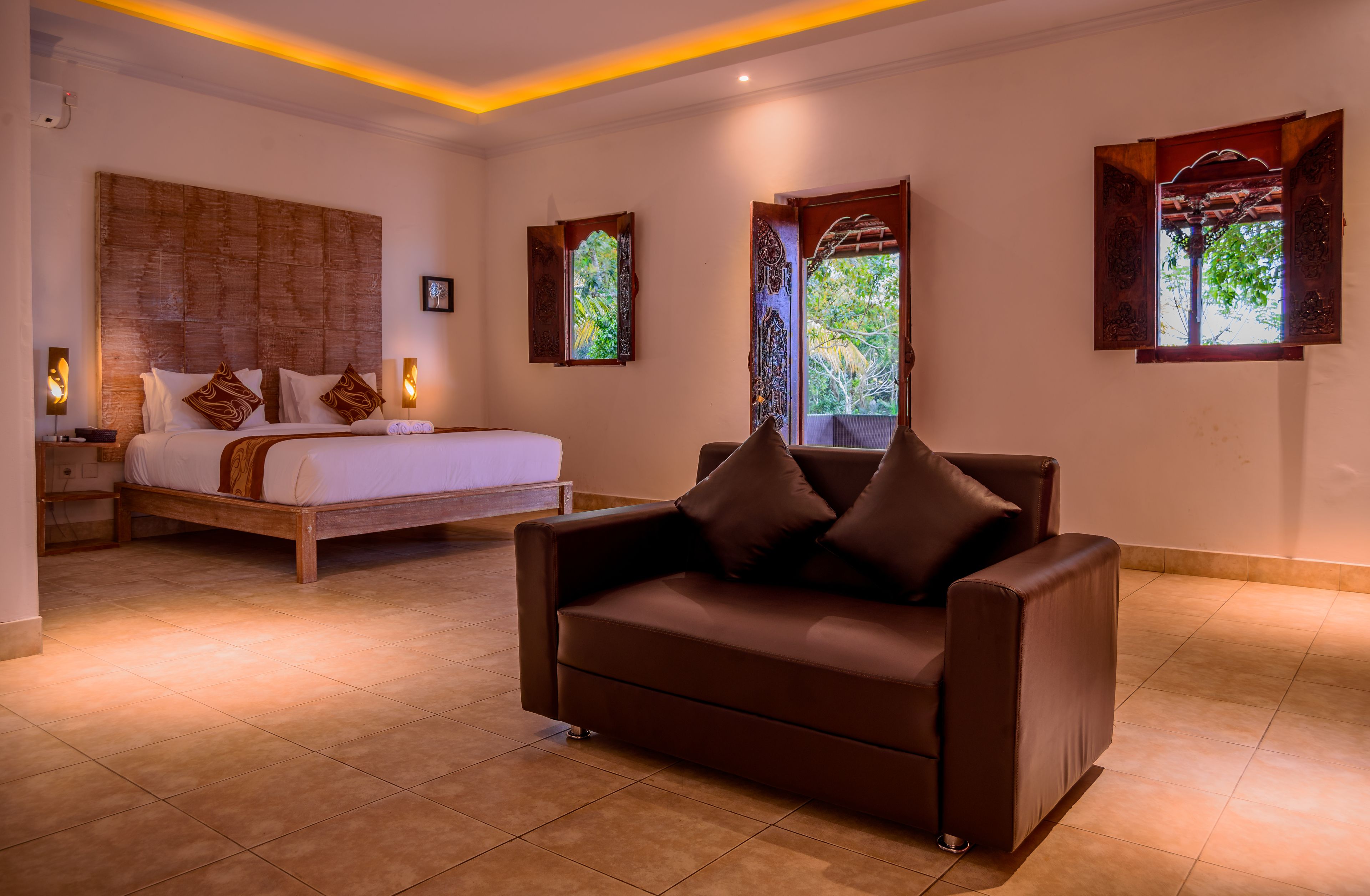 Quarto com uma cama, um sofá de couro marrom e duas janelas com molduras de madeira decorativa.