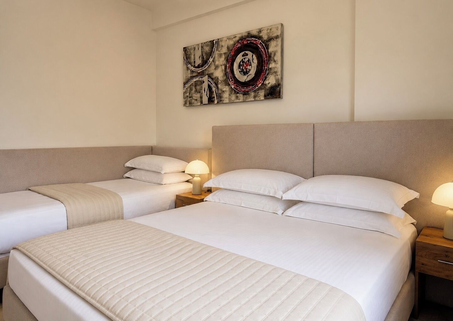 Quarto de hotel com duas camas, cabeceira, mesas de cabeceira, luminárias e uma obra de arte na parede.