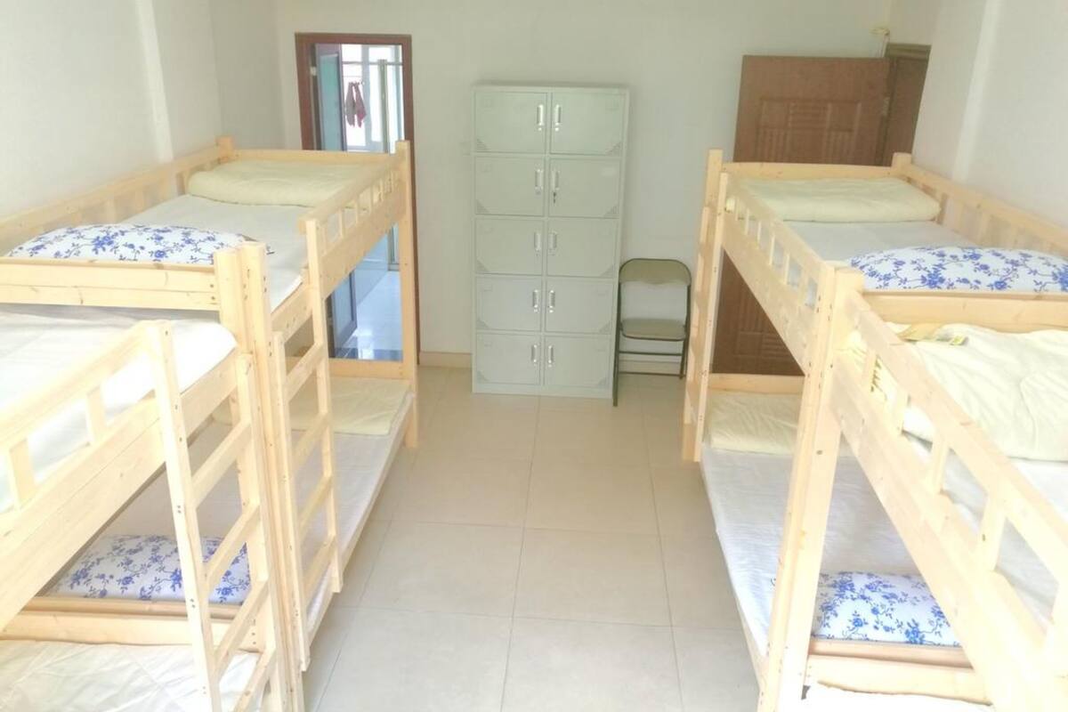 Quarto de dormitório com três beliches, um guarda-roupa e um banquinho.