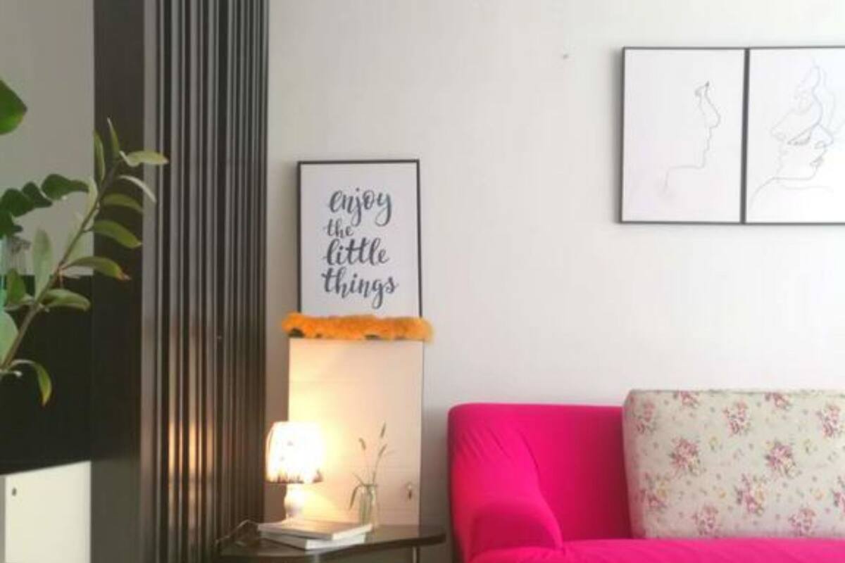 Uma sala de estar moderna com um sofá rosa vibrante, um banquinho laranja fofinho, uma luminária na parede e um pôster com uma frase motivacional.