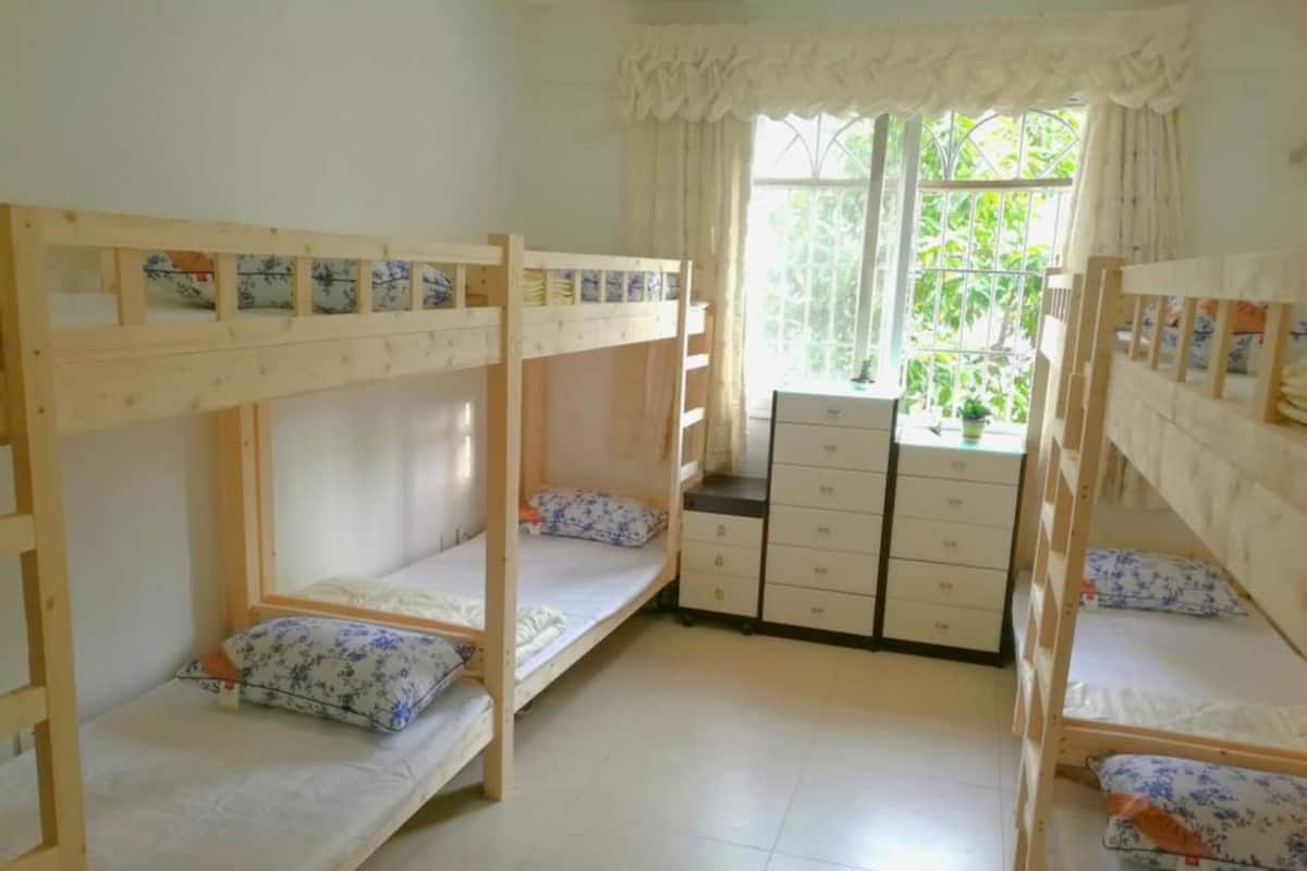 Quarto de dormitório com beliches, cômoda e janela com cortinas.