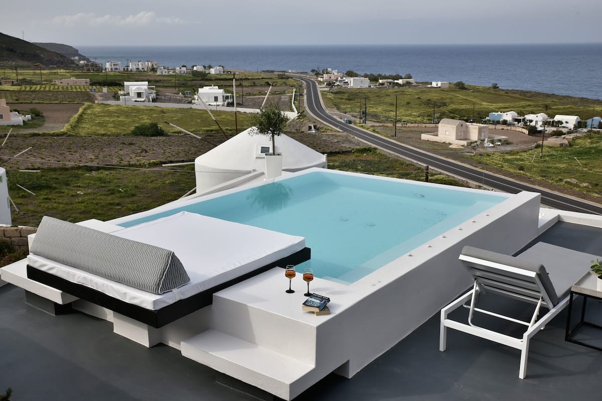 Piscina infinita moderna com um deck branco, uma espreguiçadeira e uma pequena mesa com um livro e óculos.