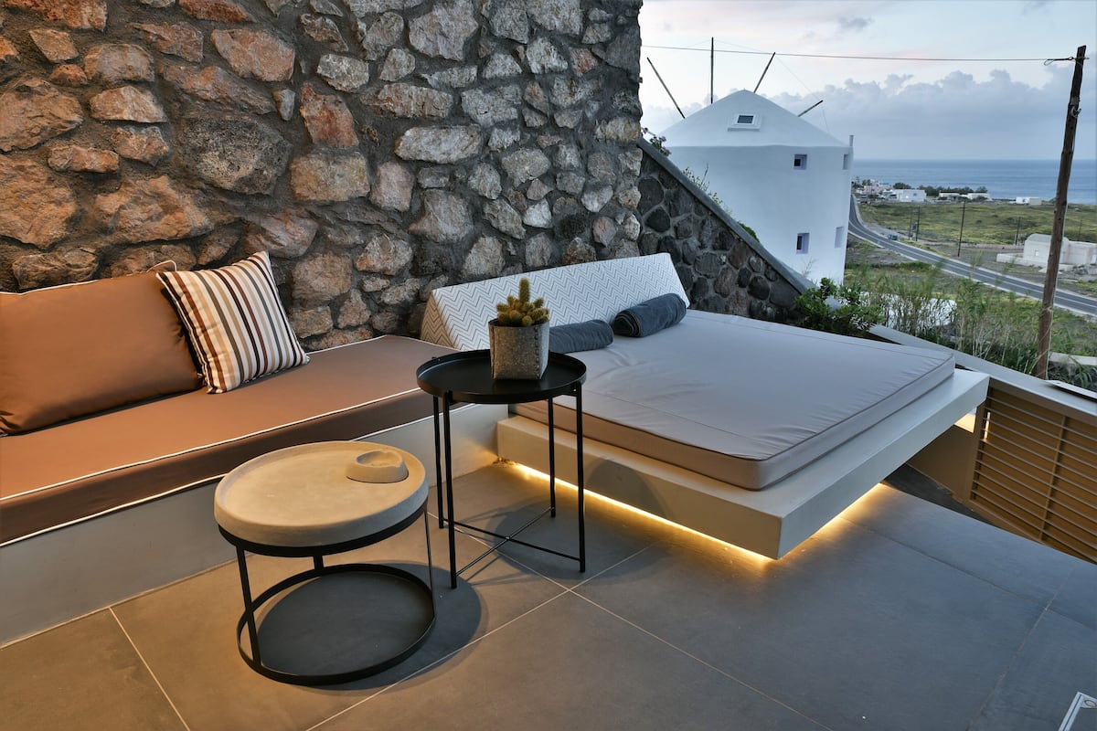 Uma varanda com sofá, uma mesa redonda pequena e uma cama com vista para o mar.