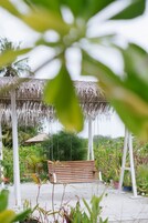 Um banco de madeira sob uma estrutura de telhado de palha, cercado por vegetação e pilares brancos.