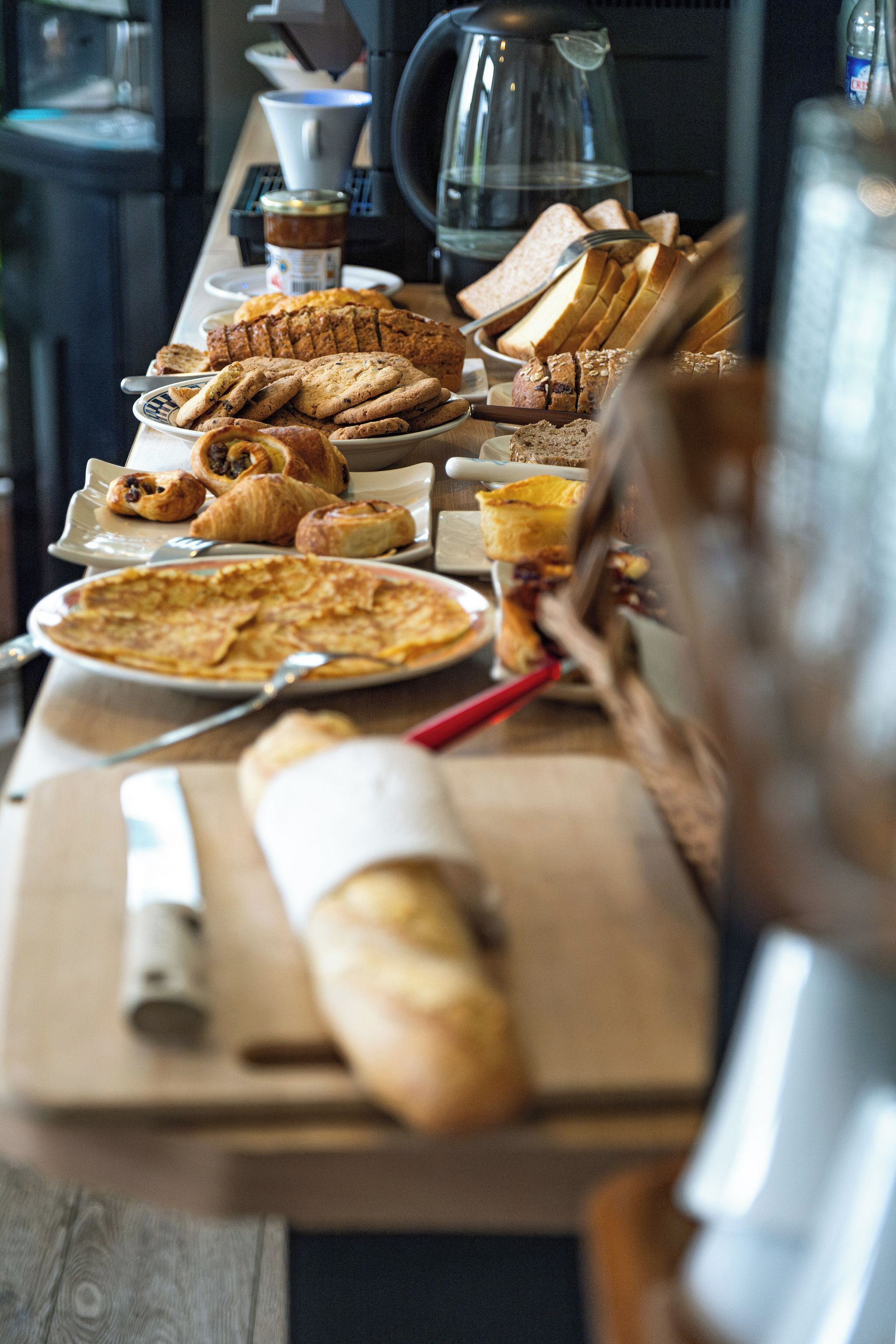 Uma mesa de café da manhã com diversos pães, doces e uma cafeteira.