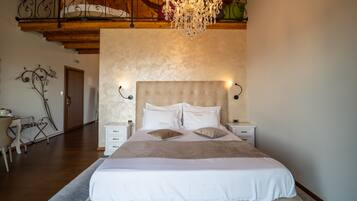 Quarto com uma cama grande, vigas de madeira no teto, um candelabro e uma mesa de cabeceira com abajur.
