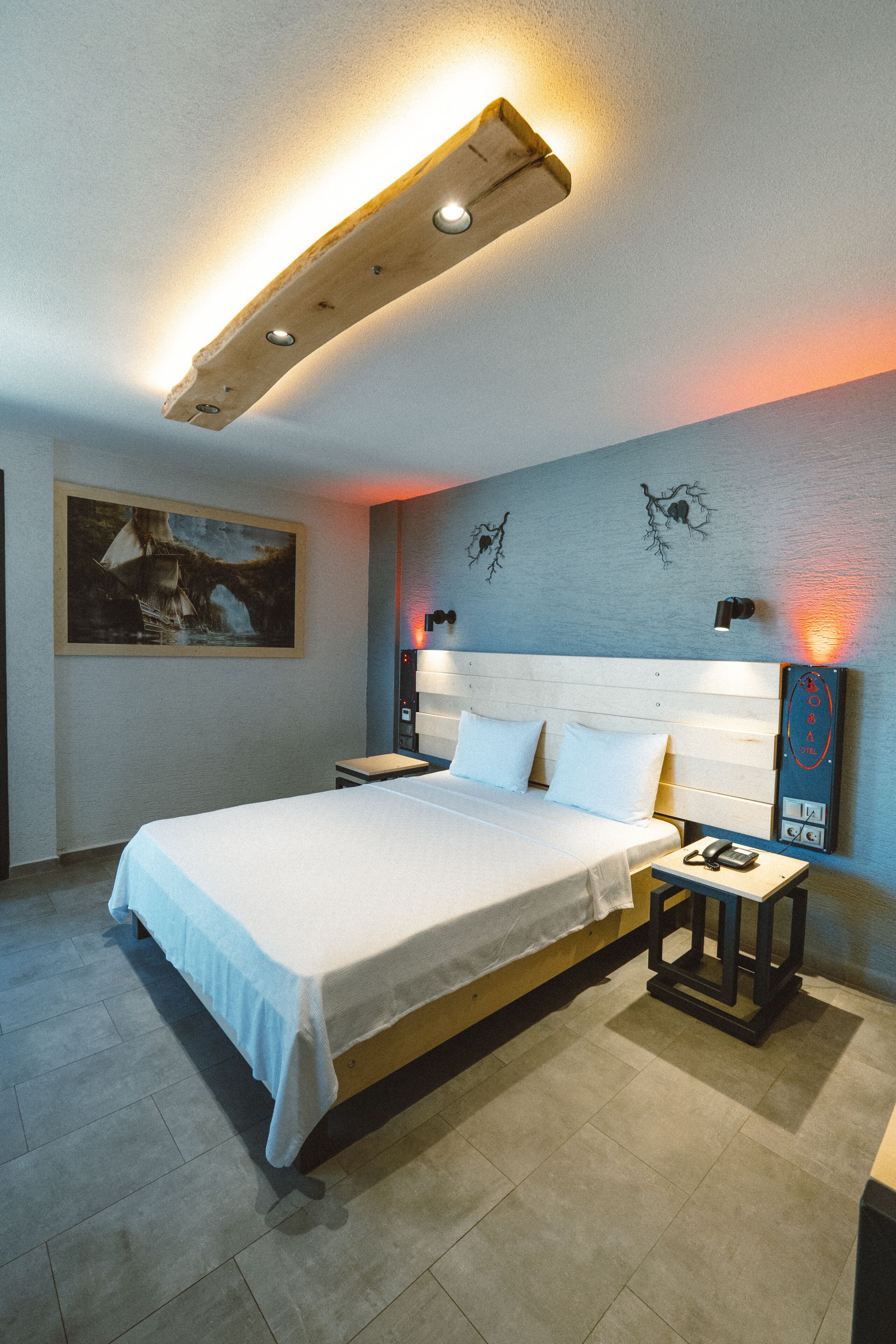 Quarto de hotel com uma cama grande, mesas de cabeceira, um quadro na parede e um lustre.