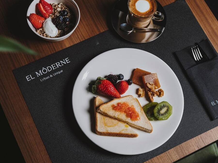 Uma mesa de madeira com torradas, frutas, uma sobremesa, uma xícara de café e um jornal para o café da manhã.