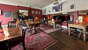 A restaurant with wooden tables and chairs, a red carpet, and a television mounted on the wall.