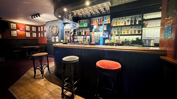 A bar area with stools, a counter, and shelves of bottles.