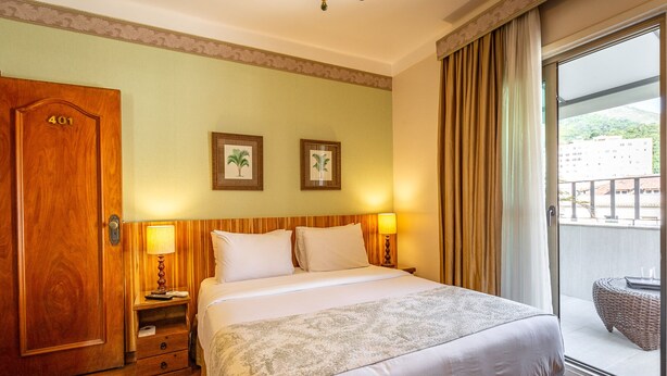 Quarto de hotel com uma cama, duas luminárias de cabeceira, uma porta com o número 401 e duas imagens emolduradas na parede.