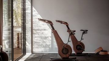 Duas bicicletas ergométricas numa sala com porta de vidro que dá para uma varanda com vista para bambus.