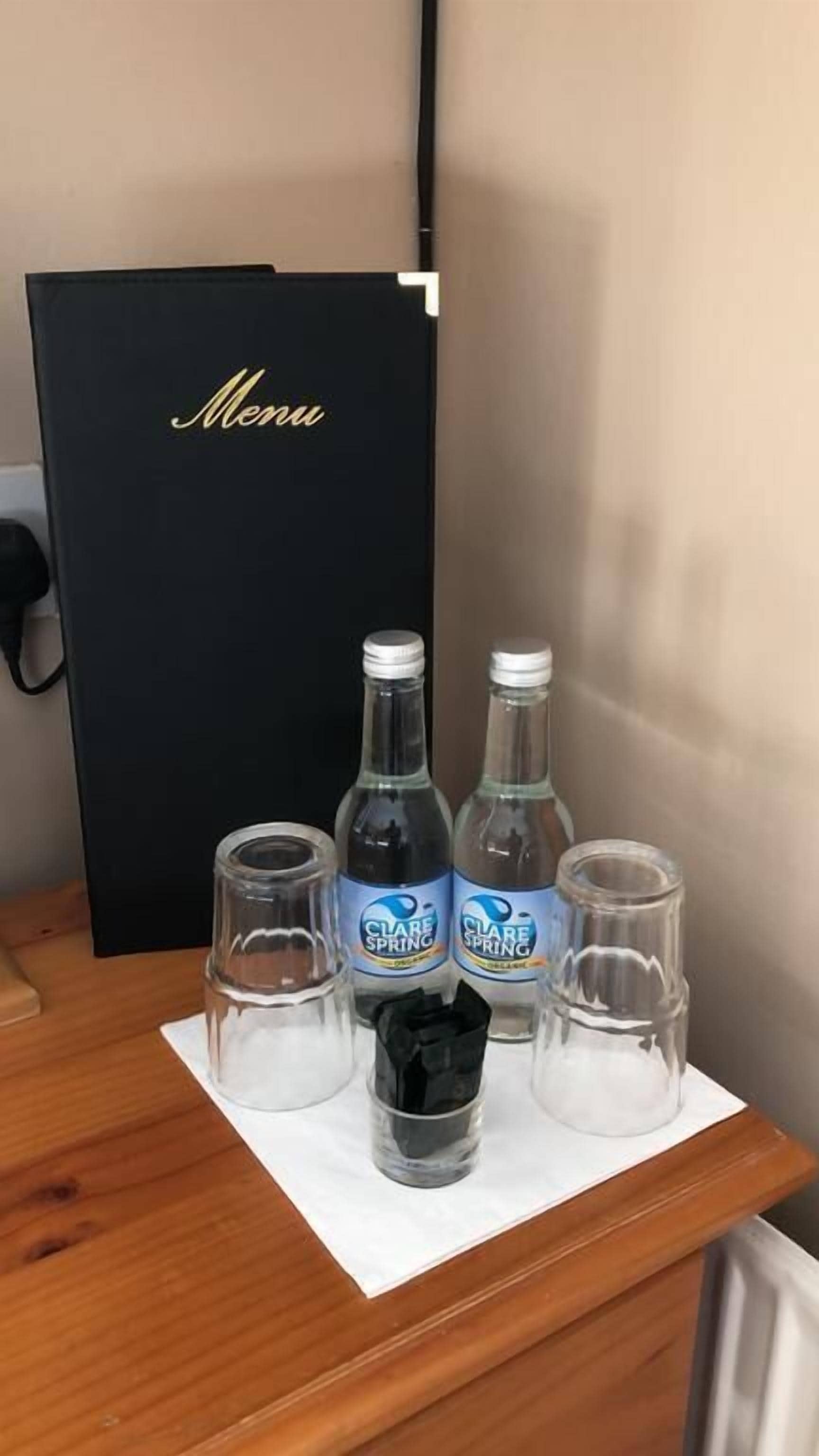 Uma mesa com quatro garrafas de água Clare Spring, um suporte de menu preto e um guardanapo branco.