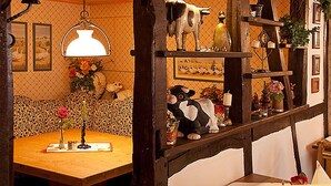 Uma área de refeições acolhedora, com uma mesa de madeira, um candeeiro pendente e uma estante com objetos decorativos, incluindo uma figurine de vaca.