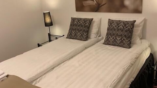 Cama de casal com duas almofadas, luminária na cabeceira e quadro de flor na parede.