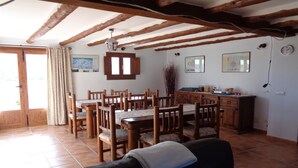 Uma sala de jantar com mesas e cadeiras de madeira, uma cozinha com armários de madeira e uma sala de estar com um sofá.