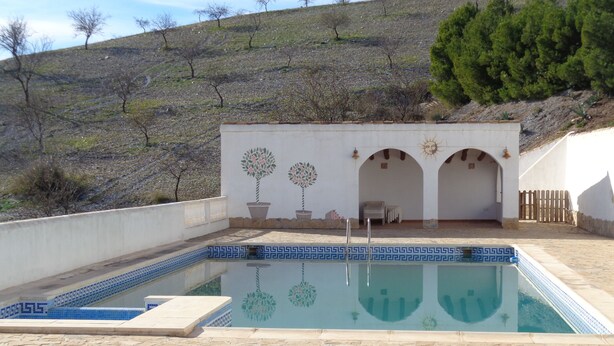 Piscina com deck revestido, área de estar coberta e um cenário de encosta.