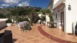Um pátio com piso de azulejos, móveis de exterior e uma pérgula coberta por trepadeiras.